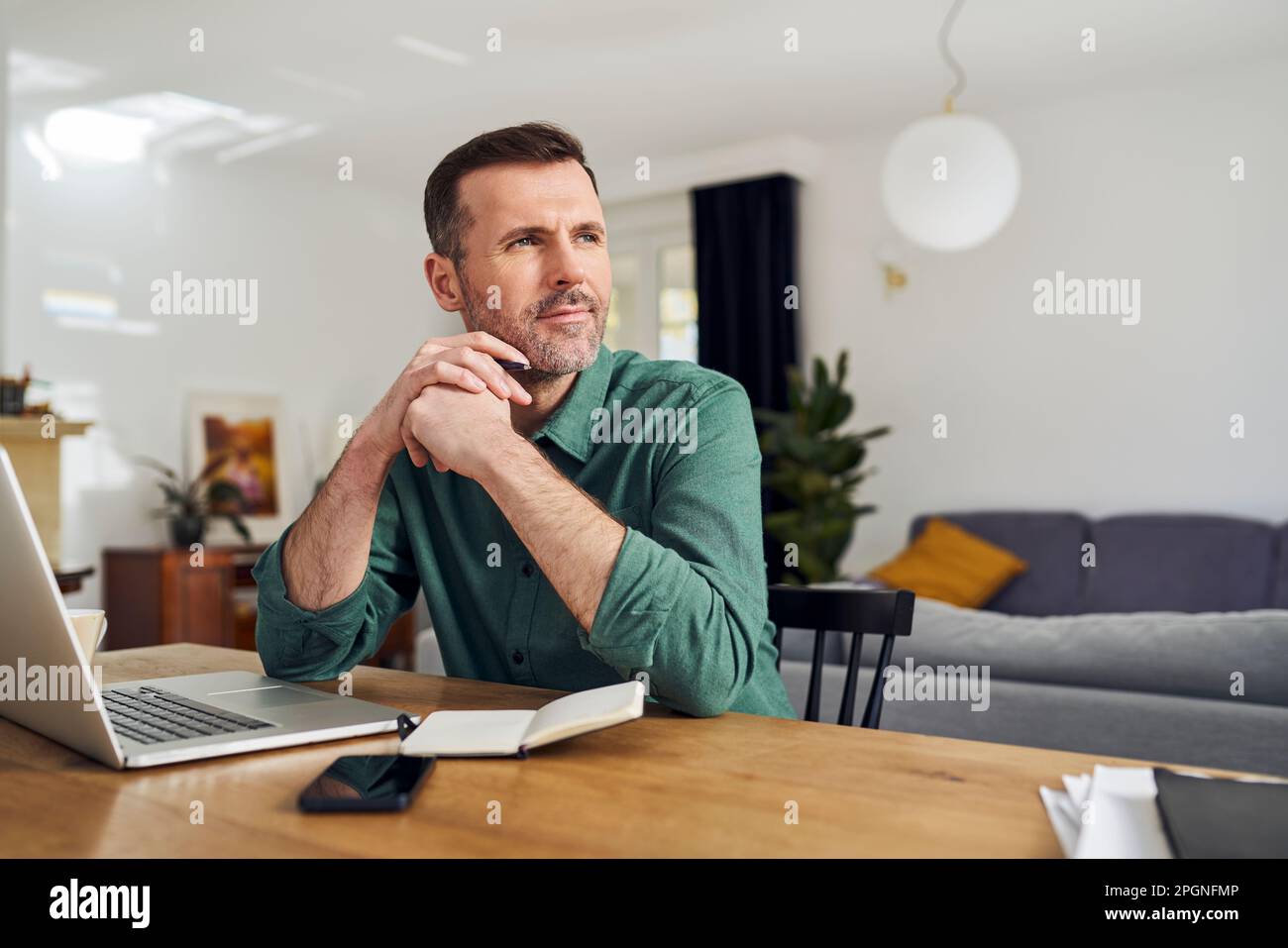 Thoughtful man sitting at table daydreaming at desk Stock Photo - Alamy