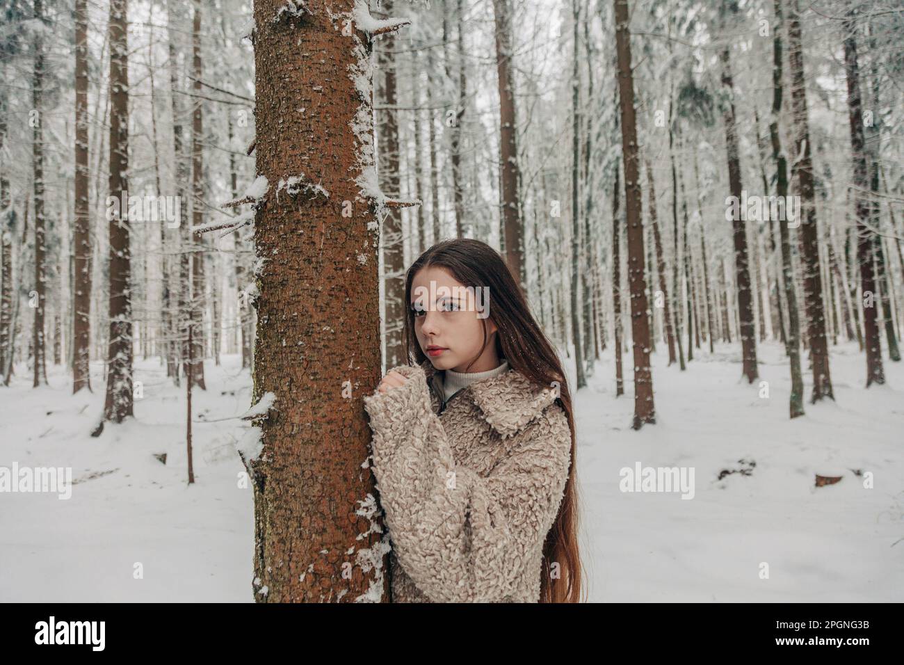 Contemplative teenage girl standing by tree in snowy forest Stock Photo ...