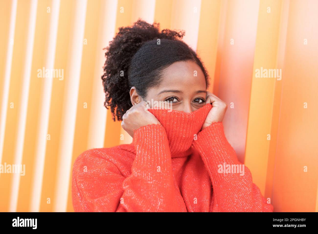 Woman covering face with turtleneck sweater by orange wall Stock Photo ...