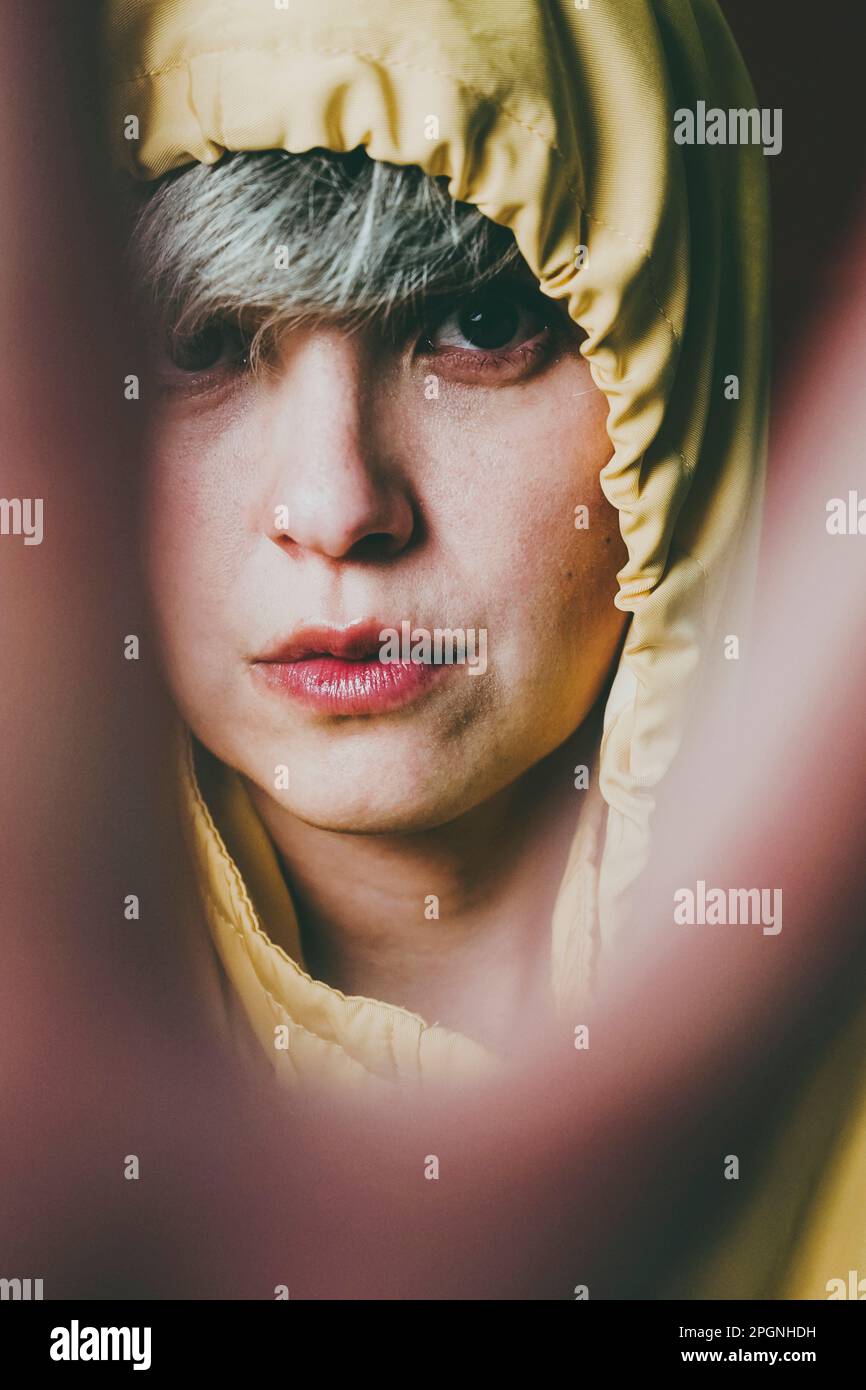 Woman wearing yellow hood seen through fingers Stock Photo - Alamy