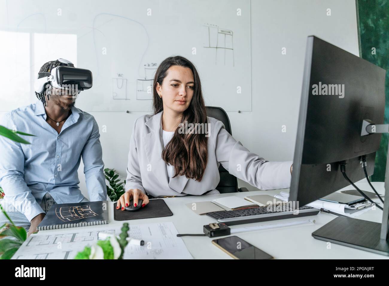 Architect using computer with colleague wearing virtual reality headset ...