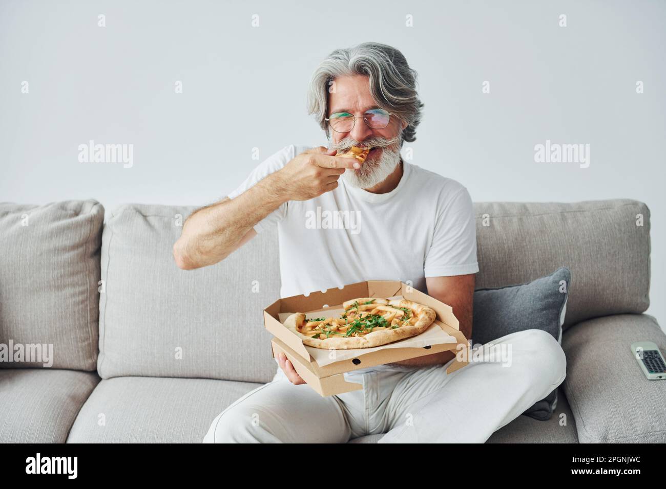 Eats delicious pizza while watching TV show. Senior stylish modern man ...