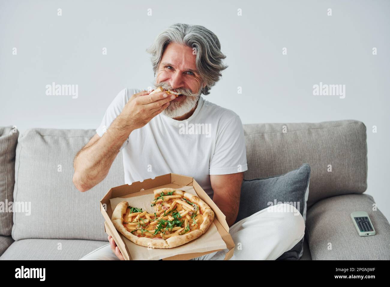 Eats delicious pizza while watching TV show. Senior stylish modern man ...
