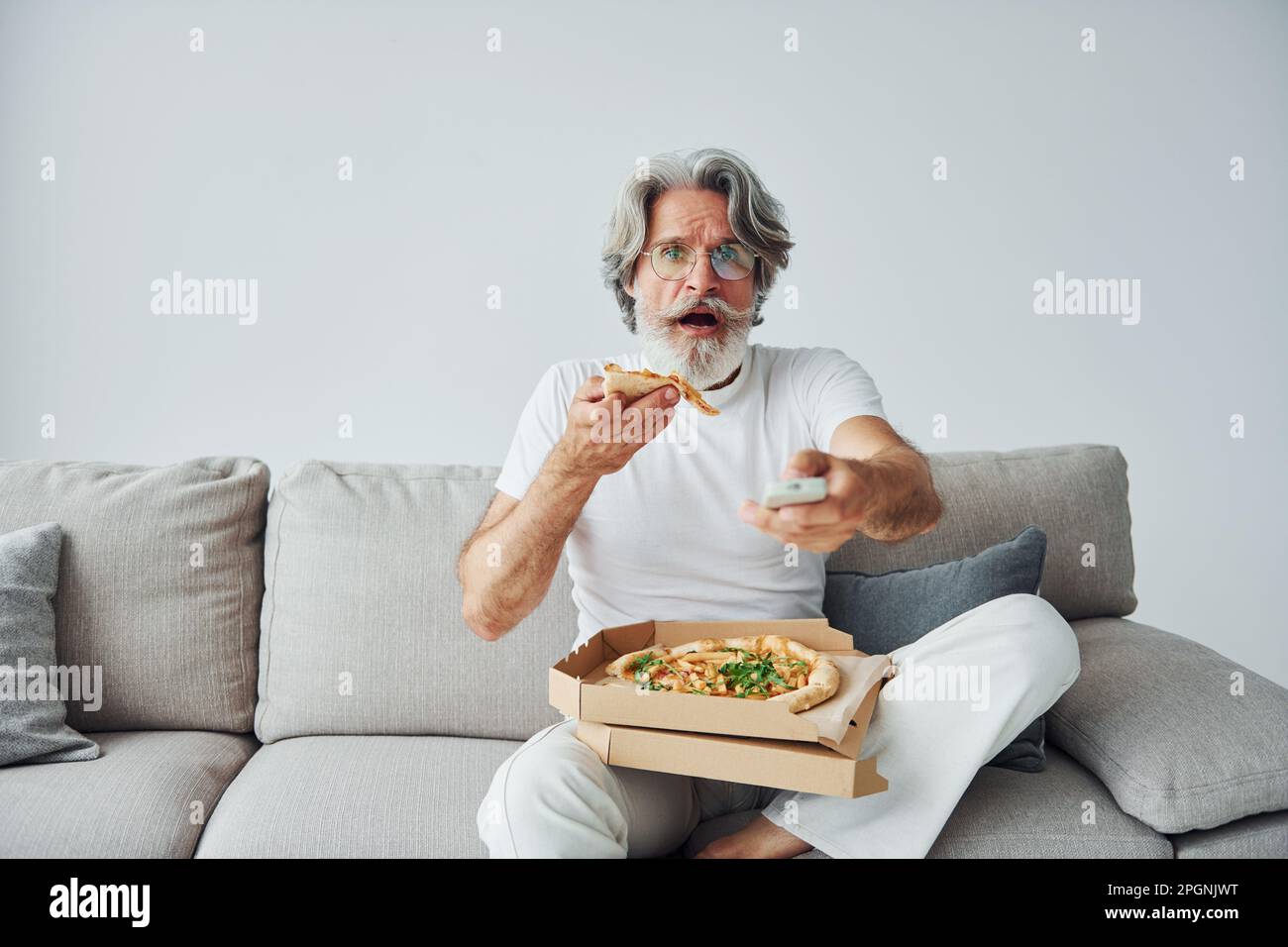Eats delicious pizza while watching TV show. Senior stylish modern man ...