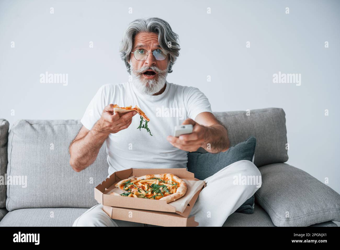 Eats delicious pizza while watching TV show. Senior stylish modern man ...