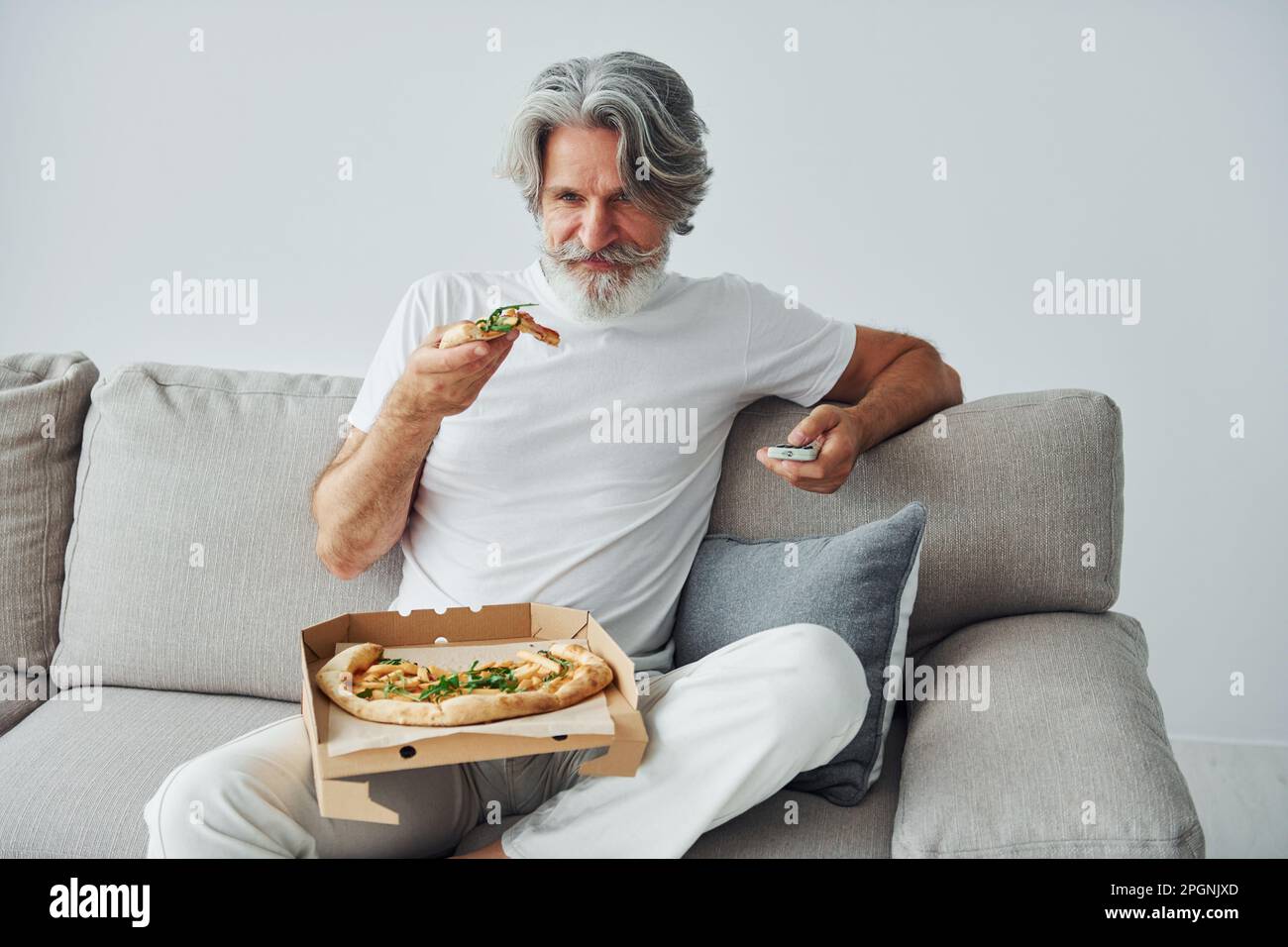 Eats delicious pizza while watching TV show. Senior stylish modern man ...