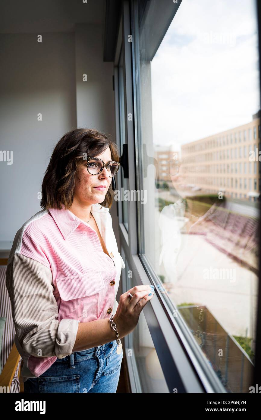 Thoughtful woman wearing eyeglasses looking through window Stock Photo ...