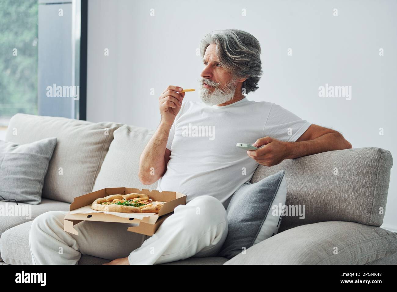Eats delicious pizza while watching TV show. Senior stylish modern man ...