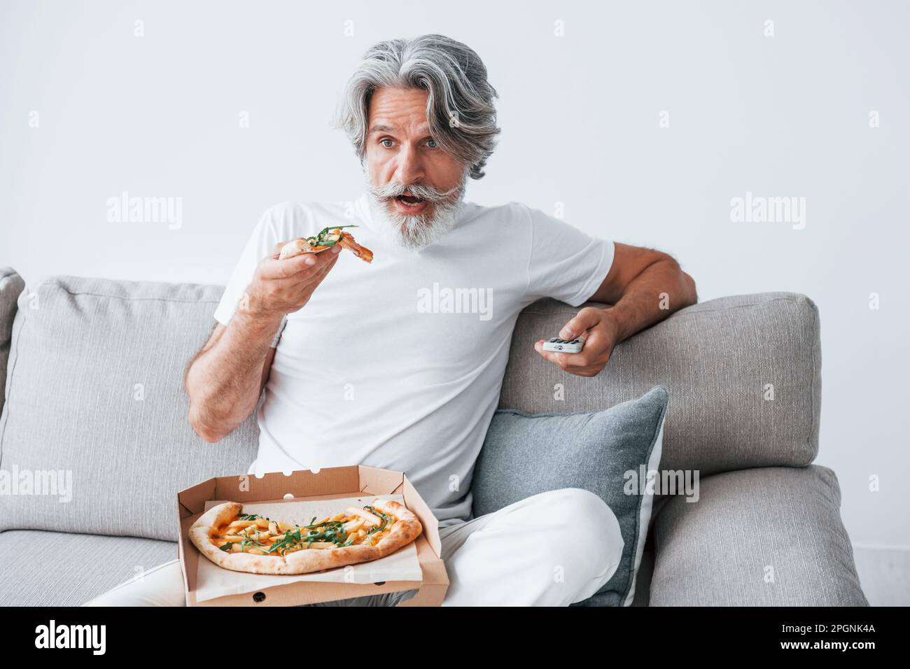Eats delicious pizza while watching TV show. Senior stylish modern man ...