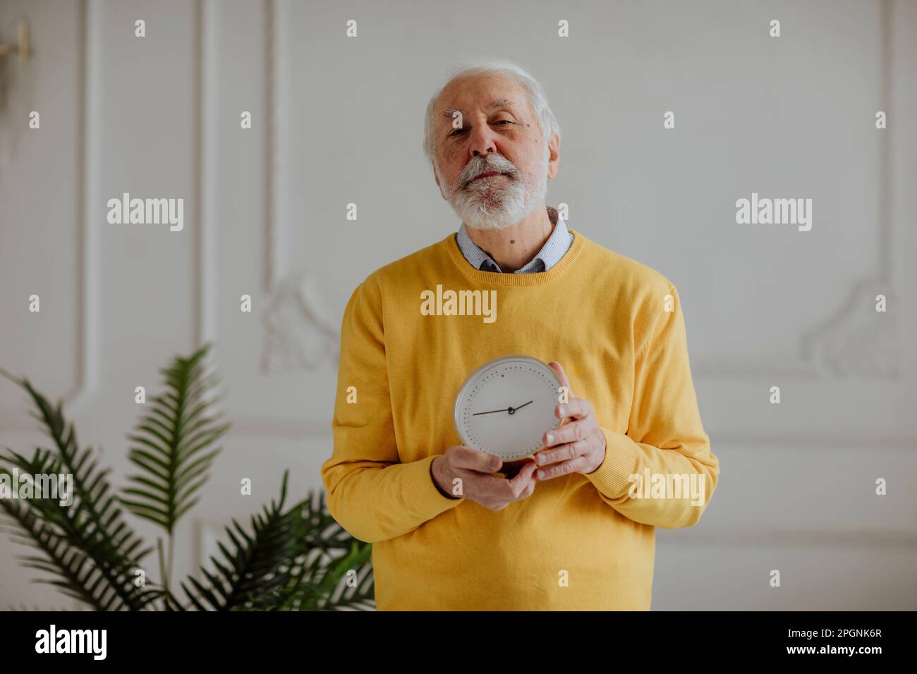 Senior man with clock standing in front of wall at home Stock Photo - Alamy