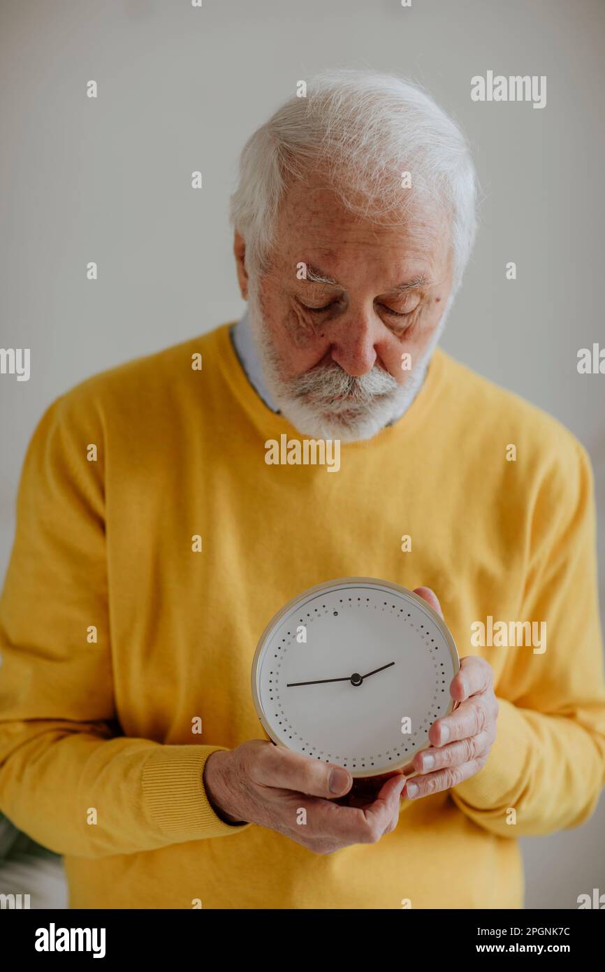 Senior man with clock standing in front of wall Stock Photo - Alamy