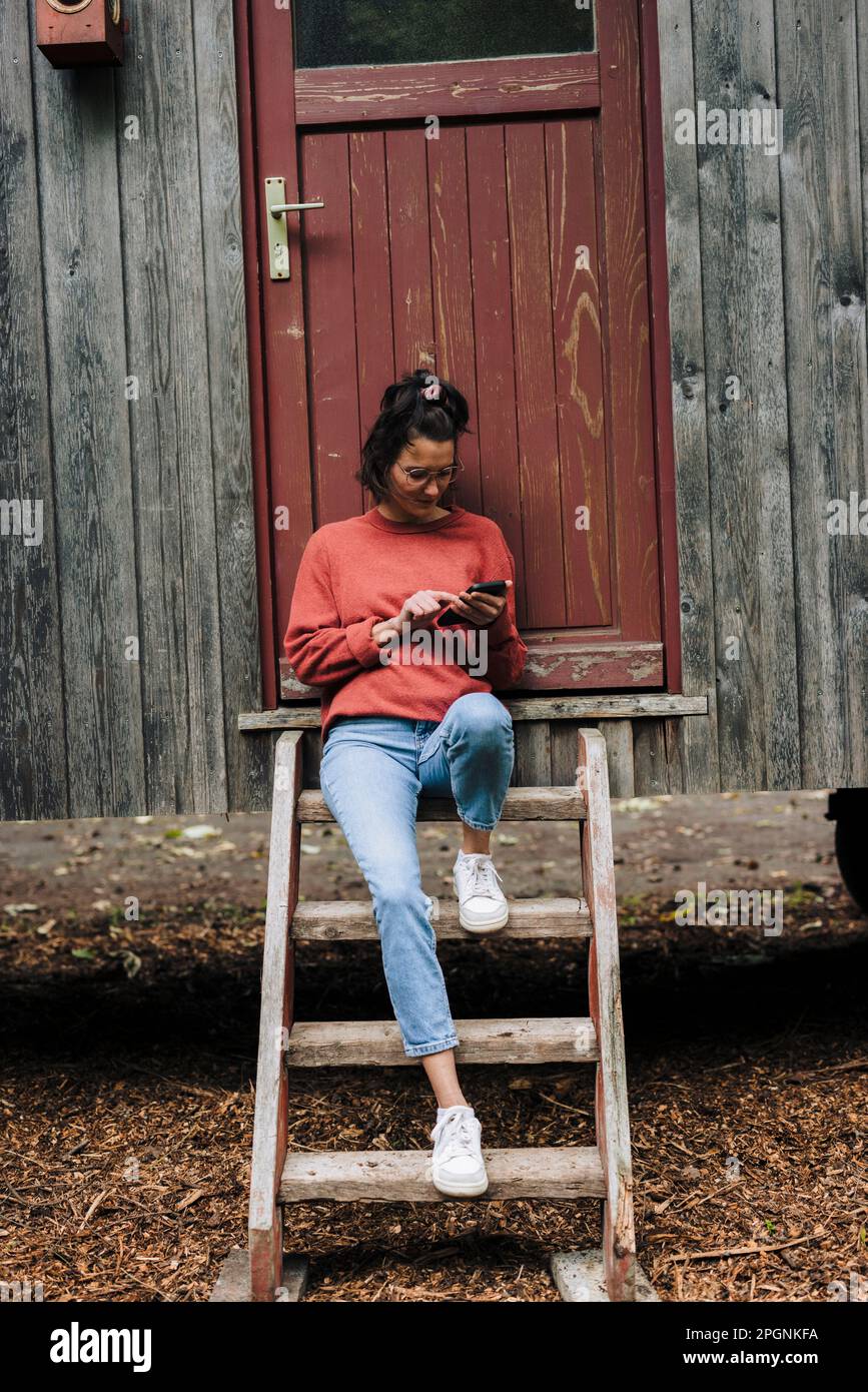 Woman using mobile phone sitting on steps in front of door Stock Photo ...