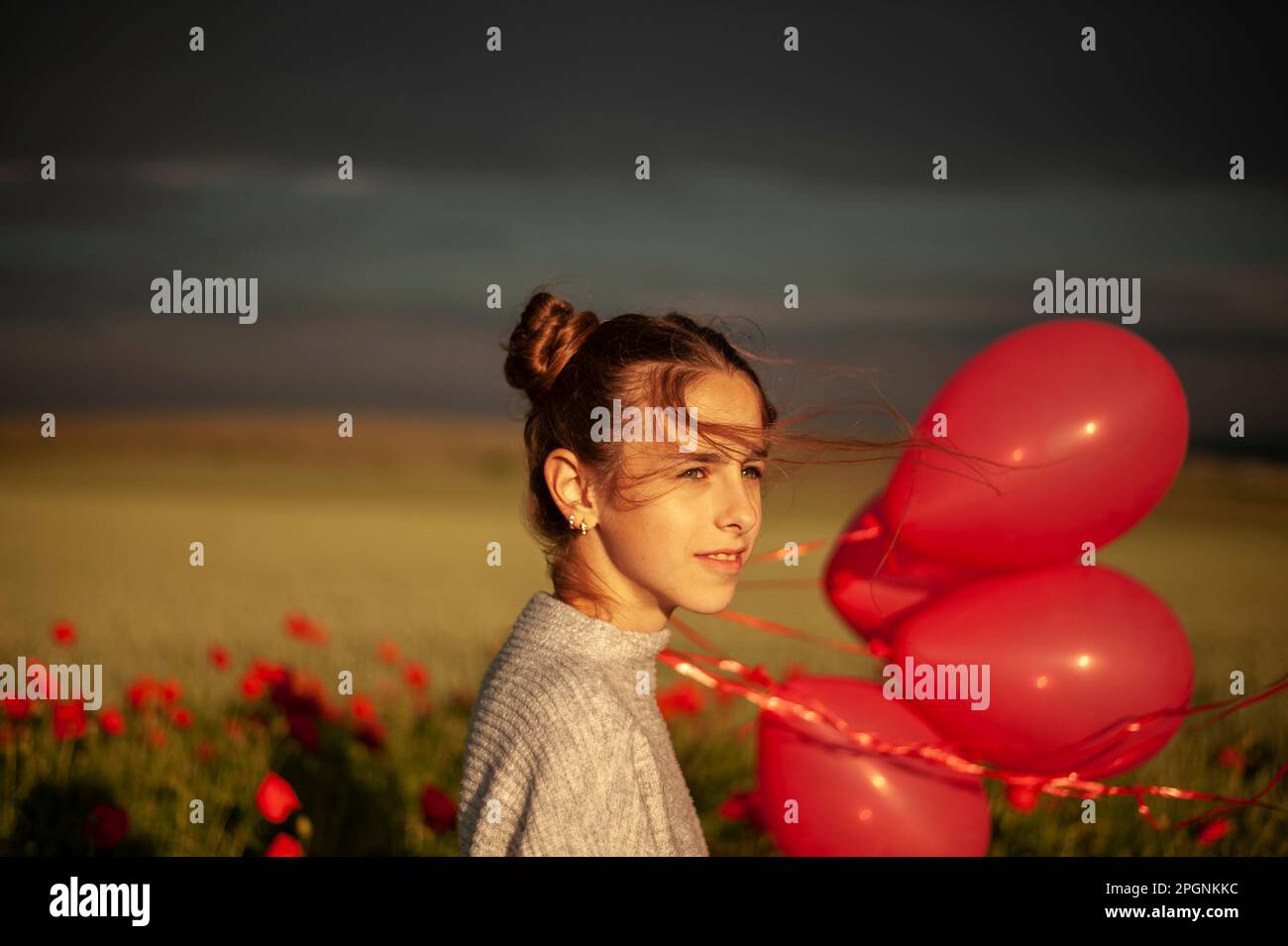 Contemplative smiling girl standing with balloons at poppy field Stock ...