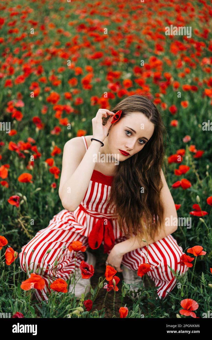 Beautiful woman crouching amidst poppy field Stock Photo - Alamy