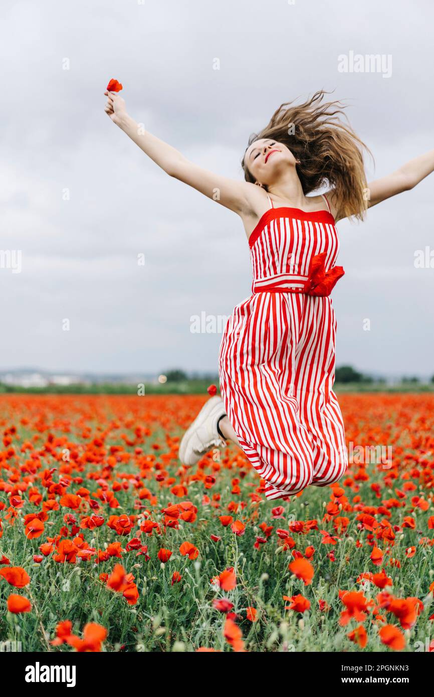 Cheerful young woman jumping at poppy field Stock Photo - Alamy