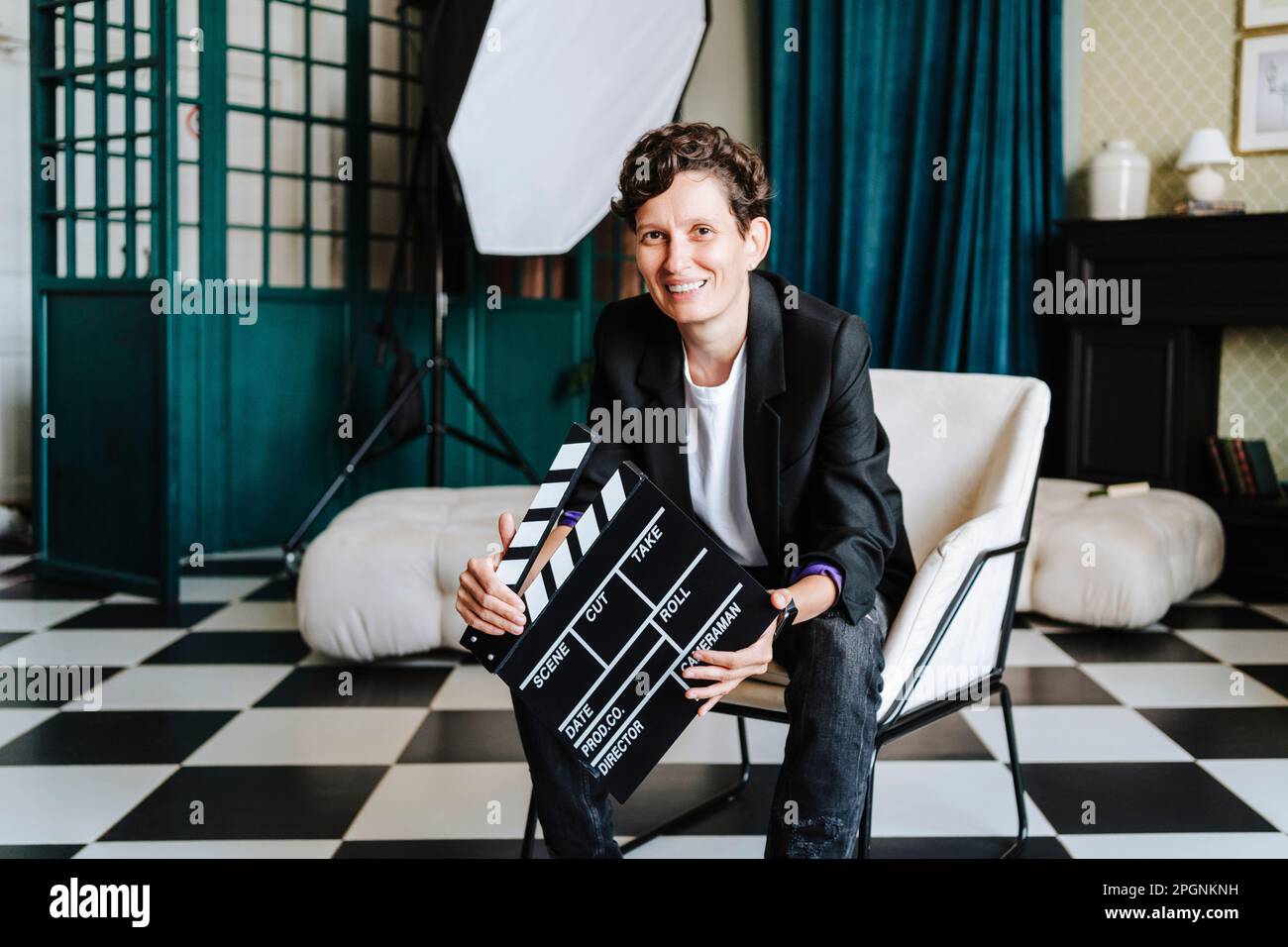 Smiling director sitting on chair holding clapboard at film set Stock ...