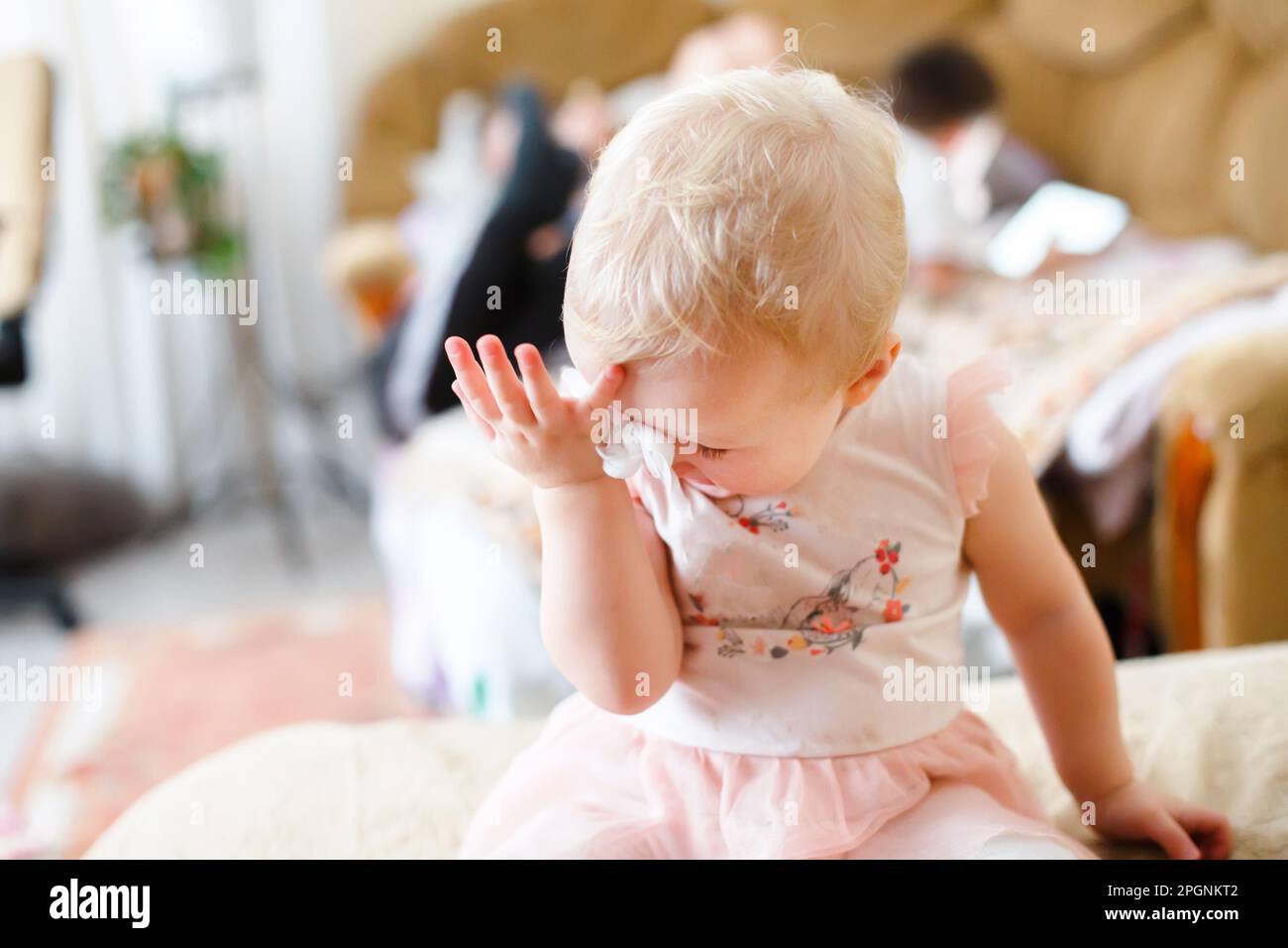 The baby wipes her nose with a napkin. the child in the apartment is ...