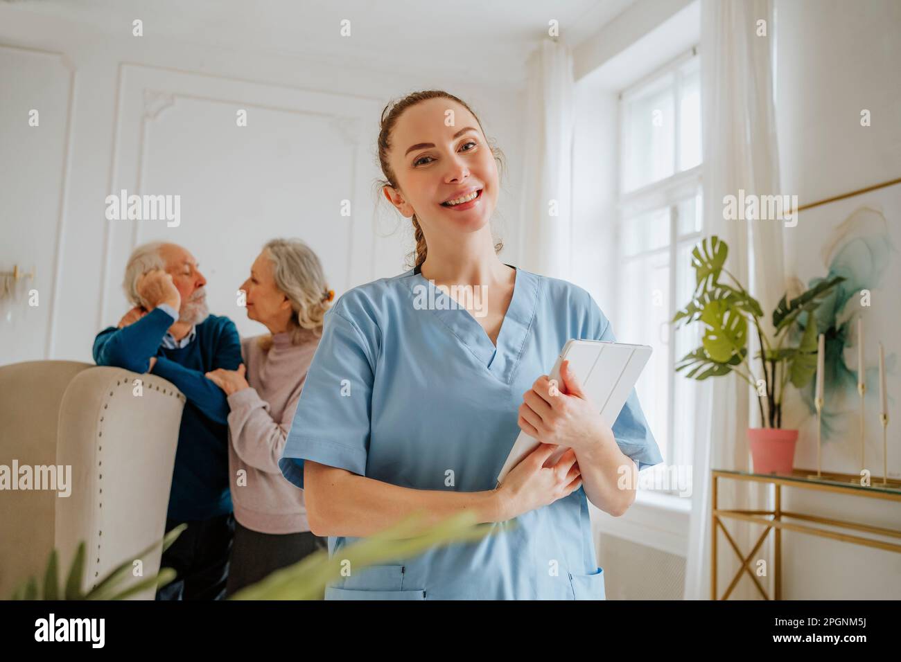 Happy nurse holding tablet PC with senior patients in background at ...