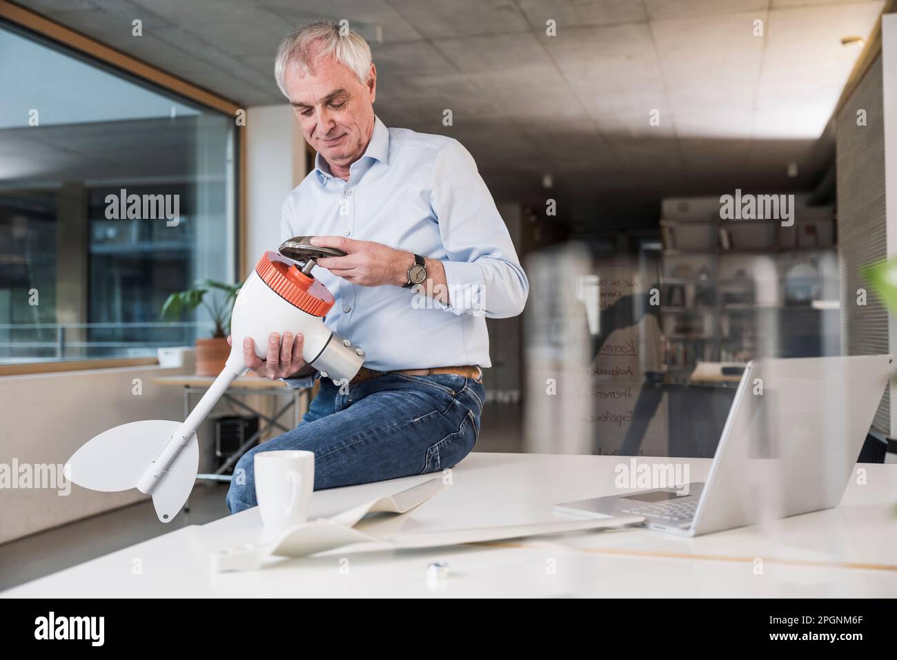 Senior engineer examining wind turbine rotor sitting on desk at office ...