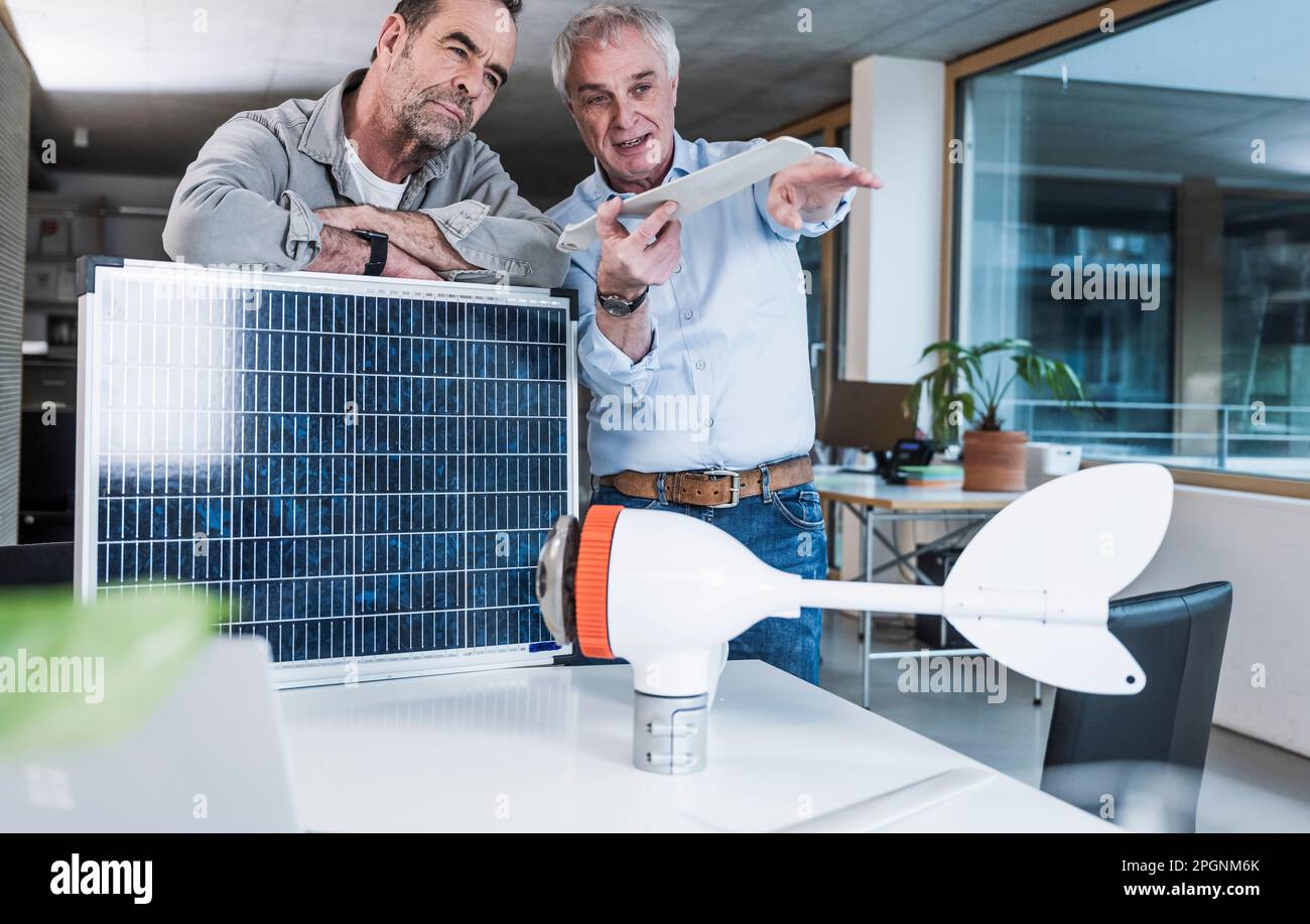 Engineer explaining wind turbine blade to colleague working at office ...