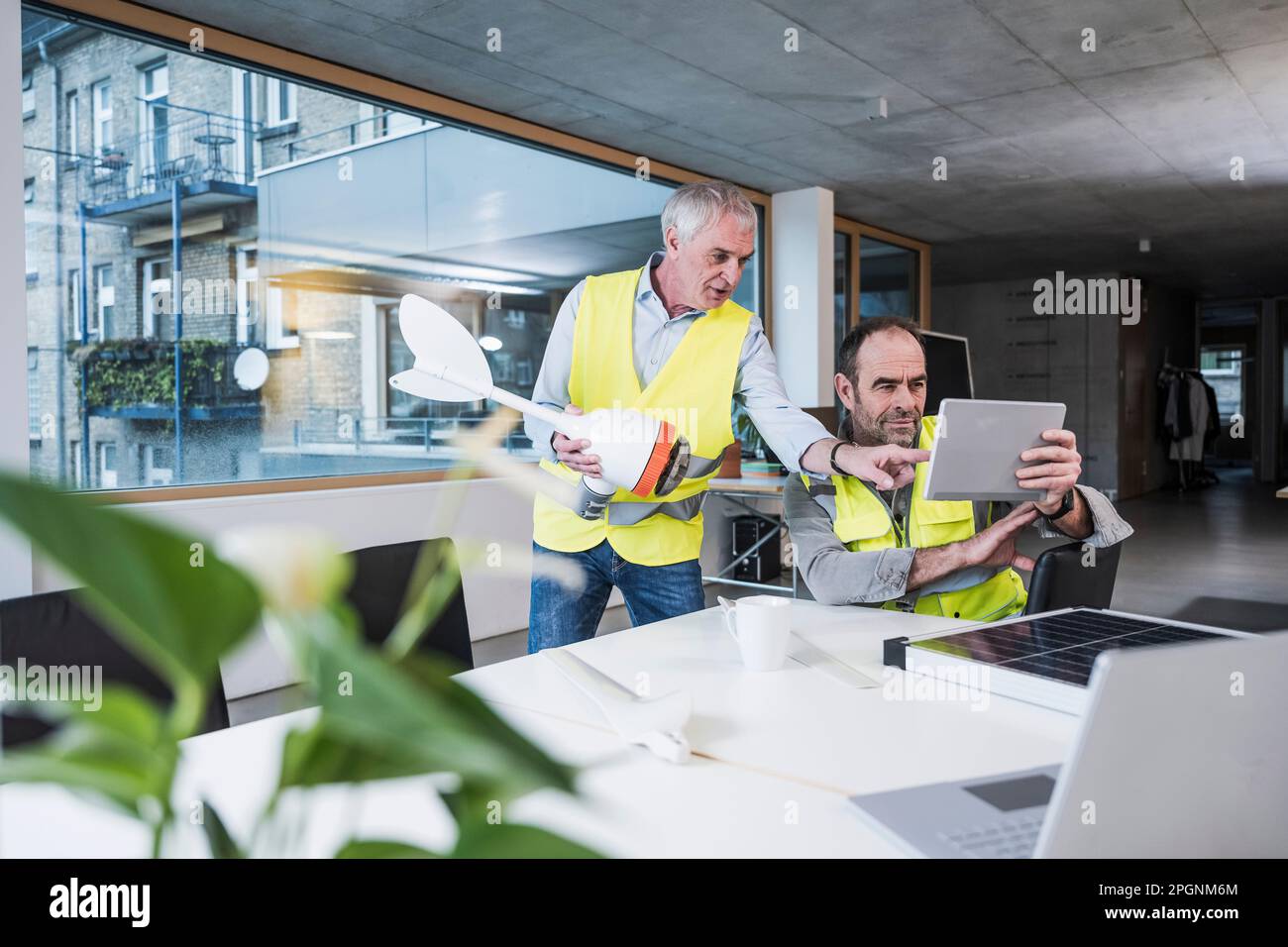 Elderly engineer with wind turbine rotor explaining colleague at office ...