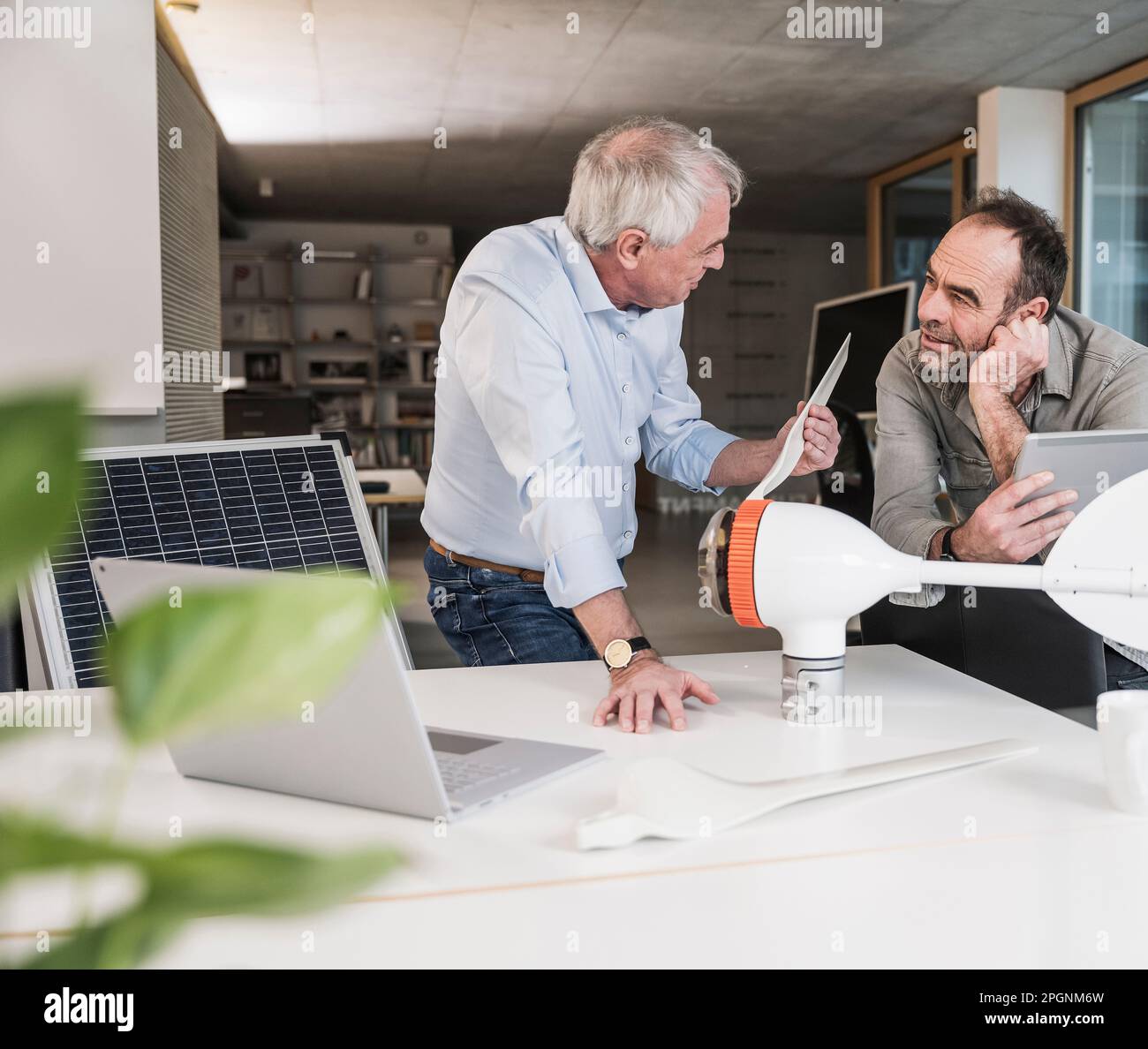 Engineer discussing with colleague over wind turbine rotor at office ...