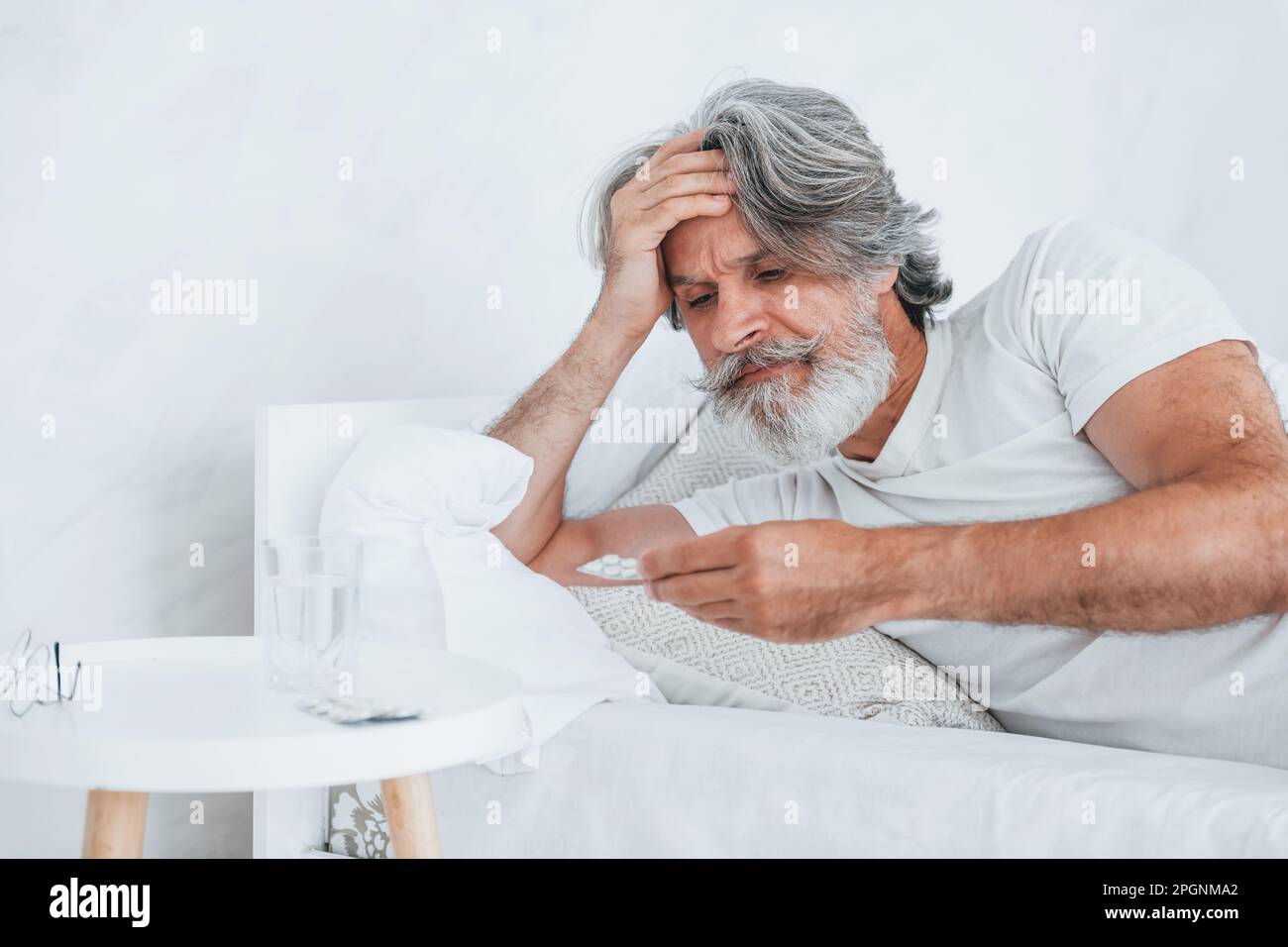 Sick senior stylish modern man with grey hair and beard indoors lying ...