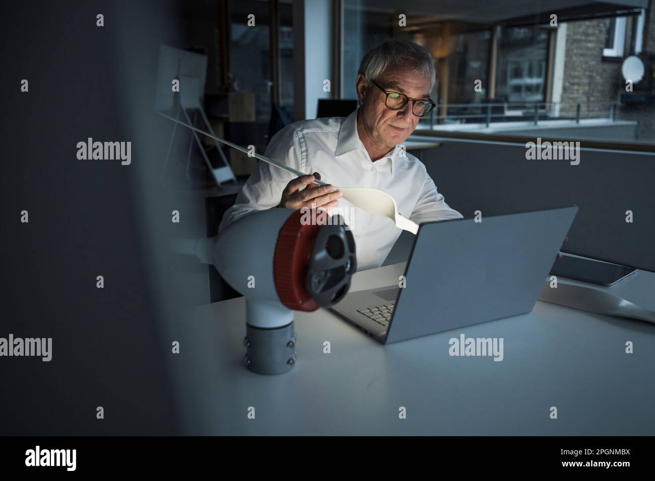 Engineer holding rotor blade and using laptop at office Stock Photo - Alamy