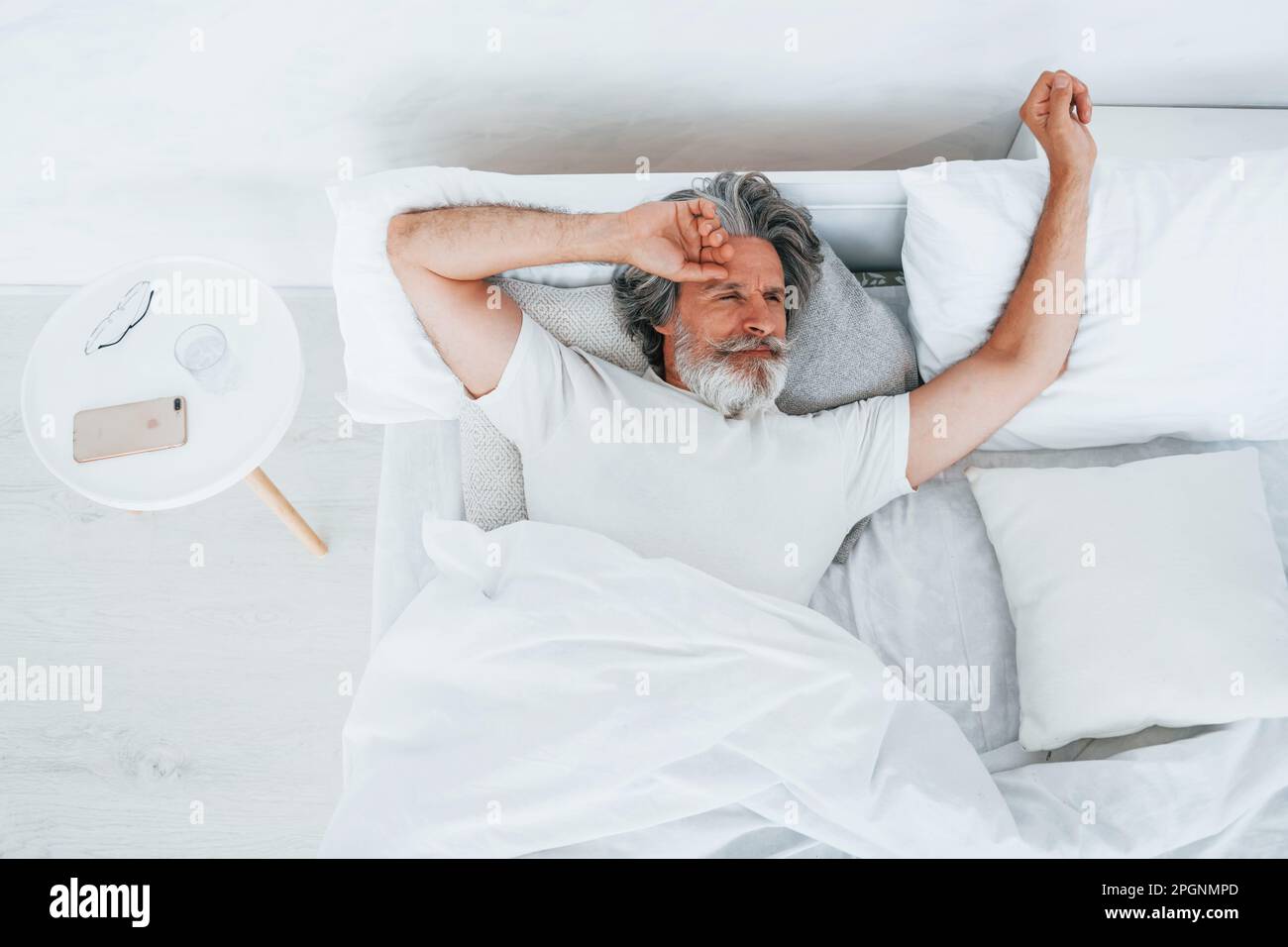 Senior stylish modern man with grey hair and beard indoors lying on the ...
