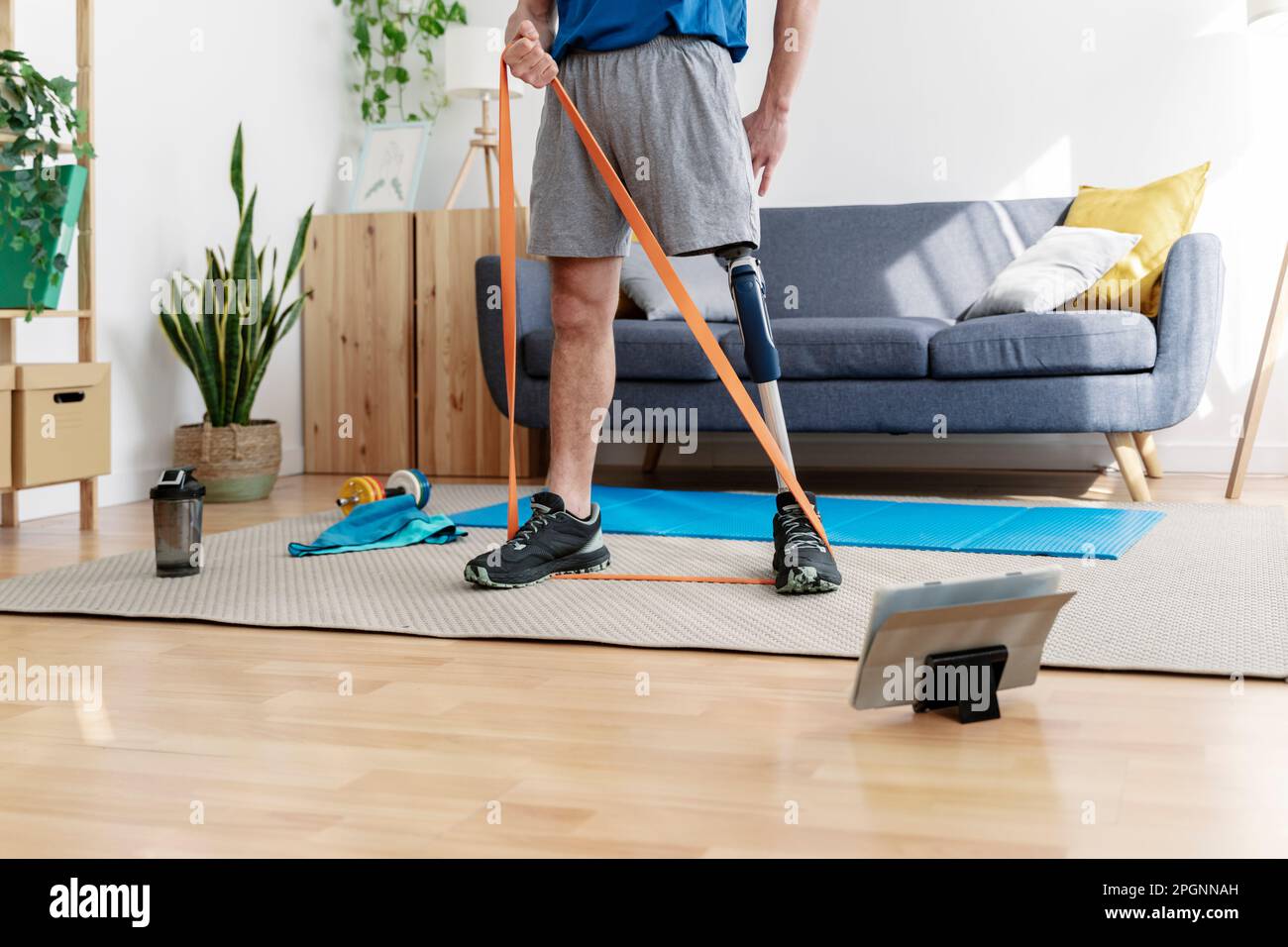 Young man with amputated leg stretching using resistance band at home ...