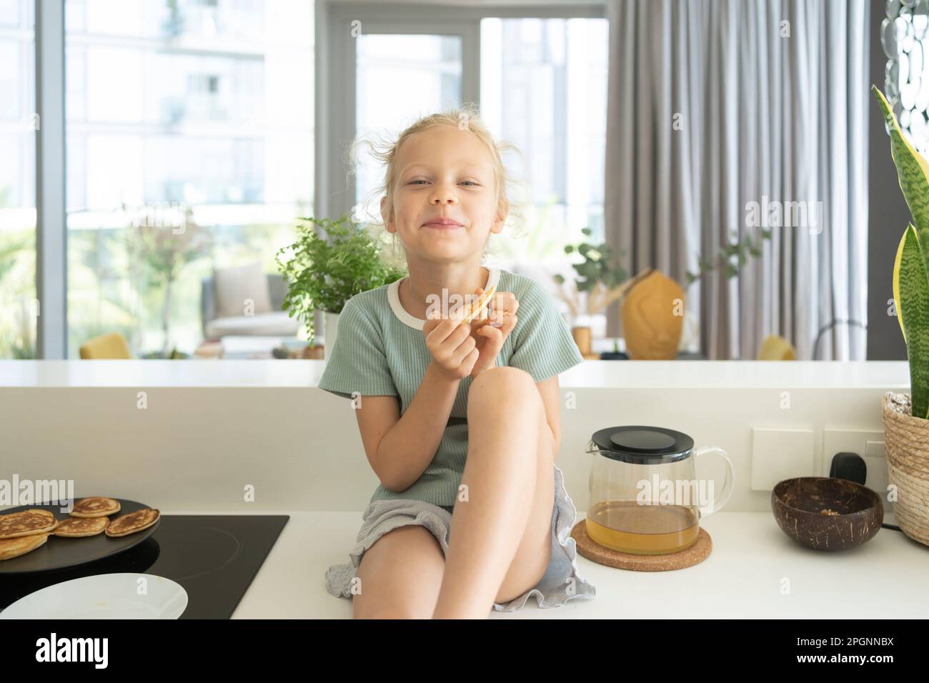 Smiling girl eating pancake sitting on kitchen counter at home Stock ...