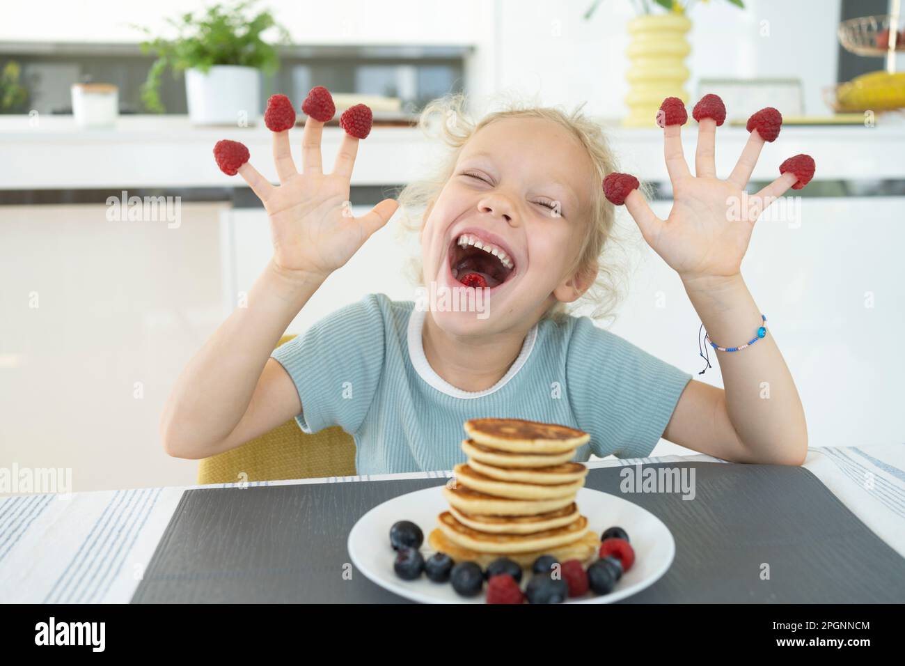 Playful girl with raspberries on fingers laughing at dining table at ...
