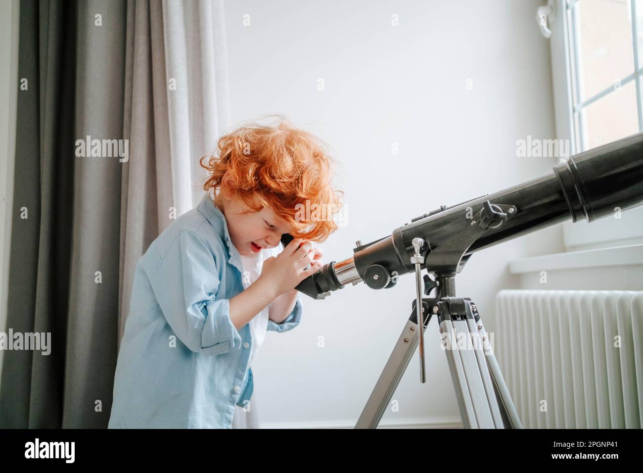Curious boy looking through telescope at home Stock Photo - Alamy