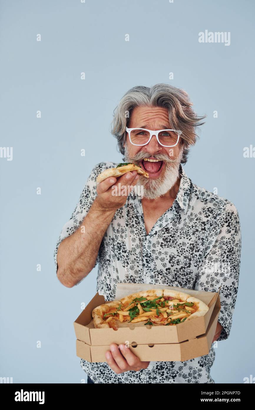 Eats pizza when standing against wall. Senior stylish modern man with ...