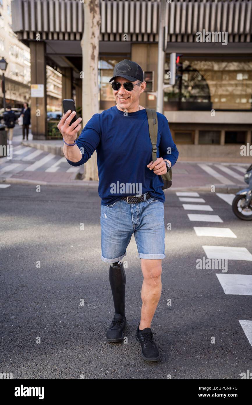 Smiling man with artificial limb taking selfie and crossing road Stock ...