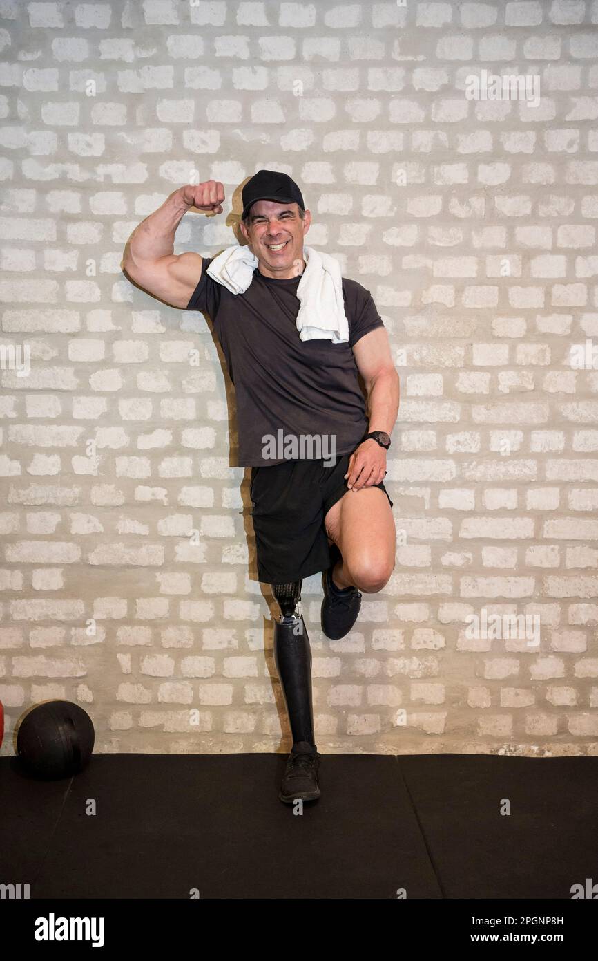 Happy man with prosthetic leg flexing muscle near wall in gym Stock ...