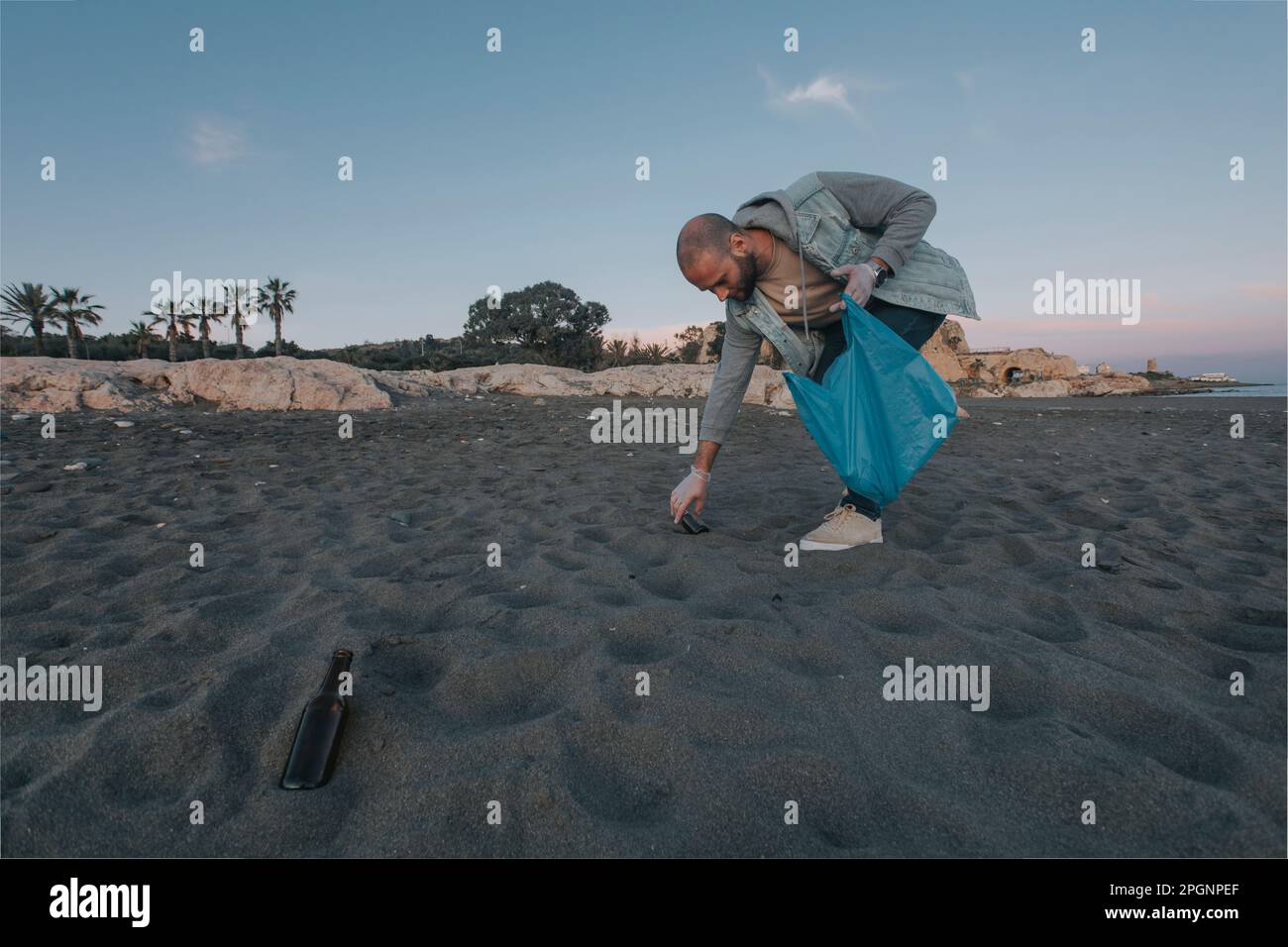 Man collecting trash in plastic bag from beach Stock Photo - Alamy