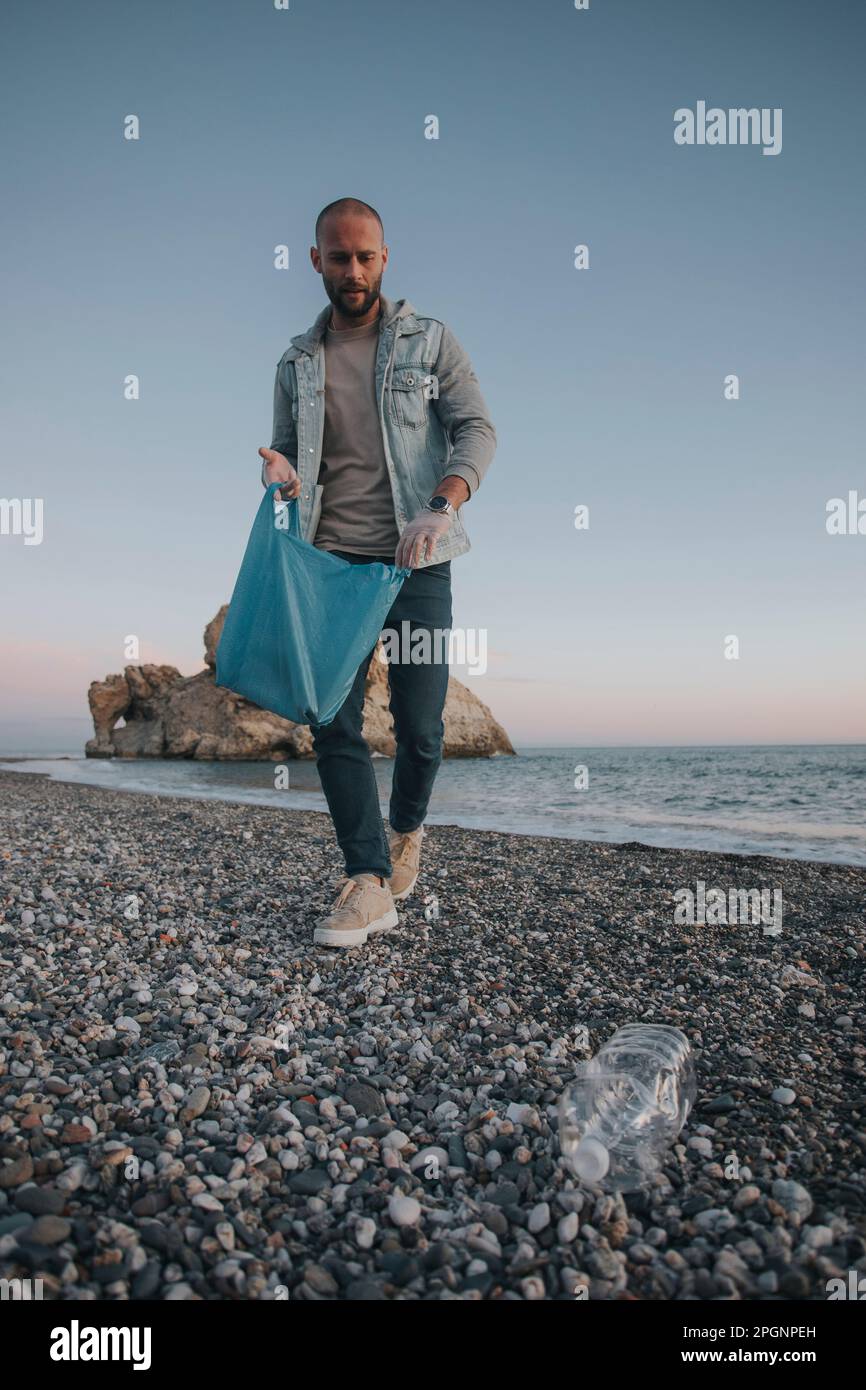 Man with plastic bag collecting trash from beach Stock Photo - Alamy