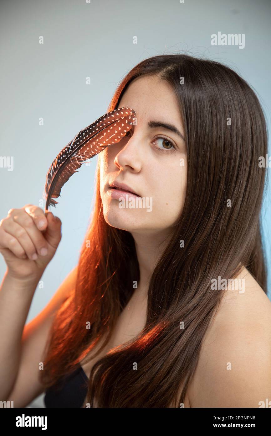 Young woman touching face with feather in front of wall Stock Photo - Alamy