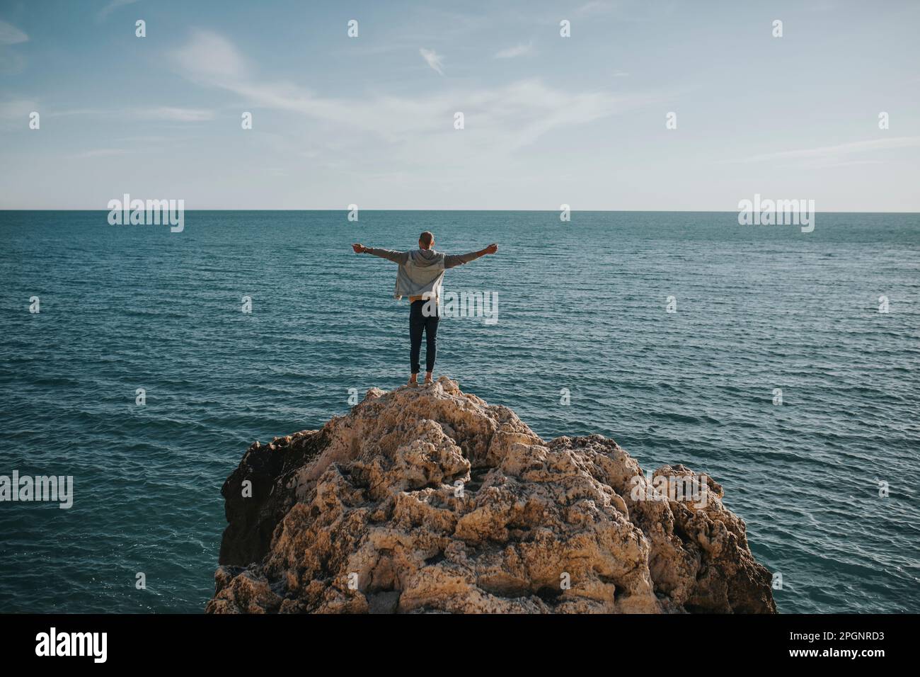Carefree man standing with arms stretched on rock in front of sea Stock ...