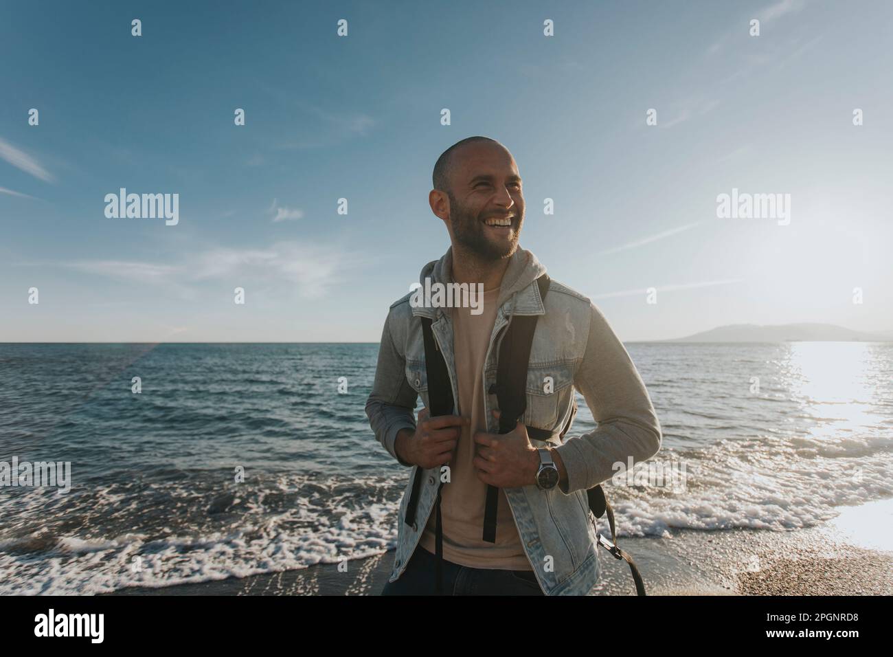 Happy man with backpack standing in front of sea Stock Photo - Alamy