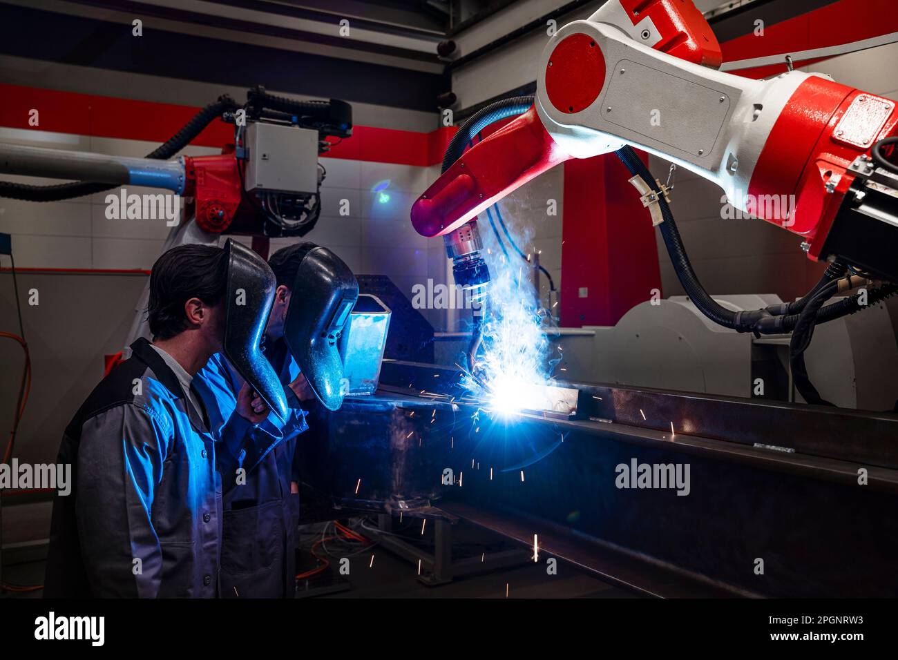 Engineers wearing protective workwear by robotic arm welding in factory ...