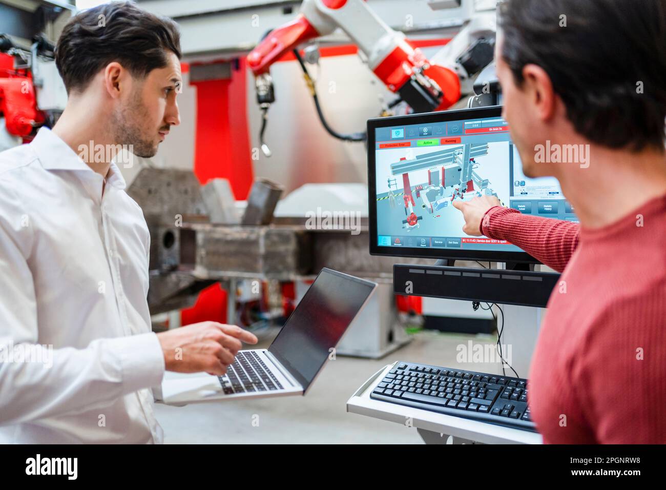 Engineer explaining colleague holding laptop at robot factory Stock ...