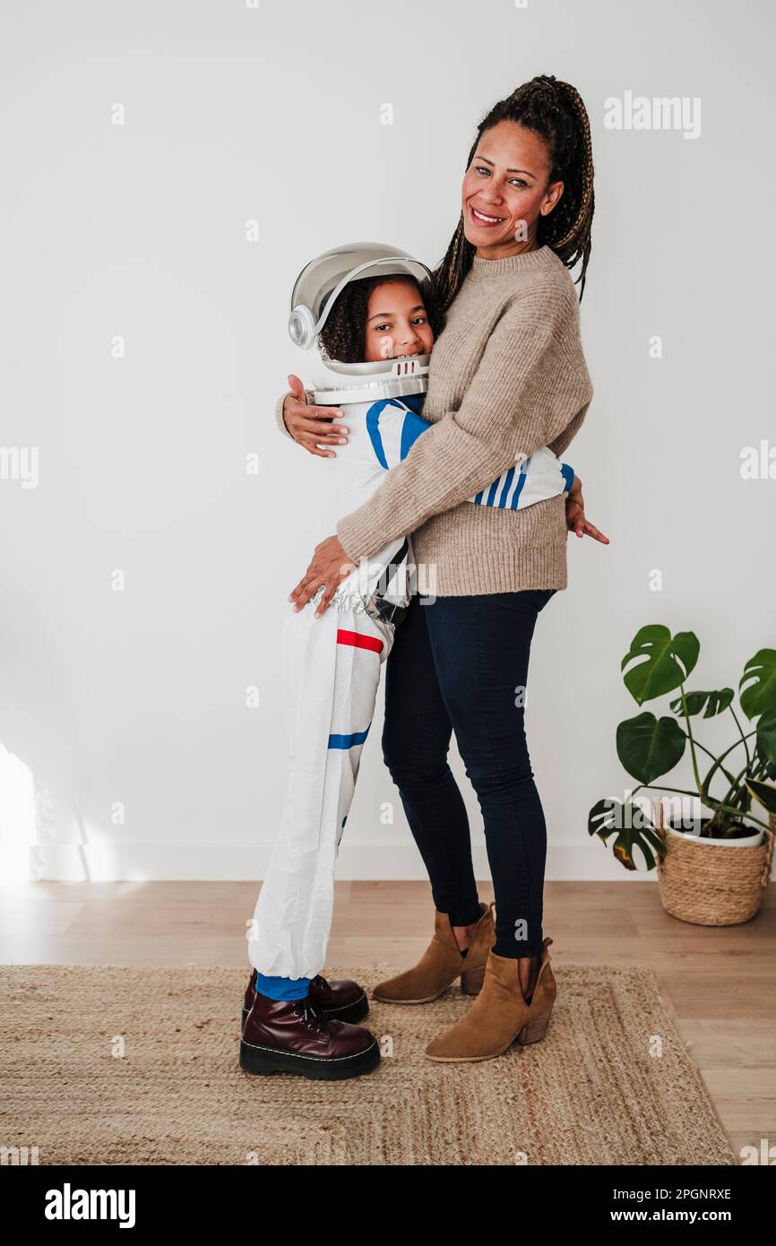 Smiling girl wearing space suit embracing mother standing at home Stock ...