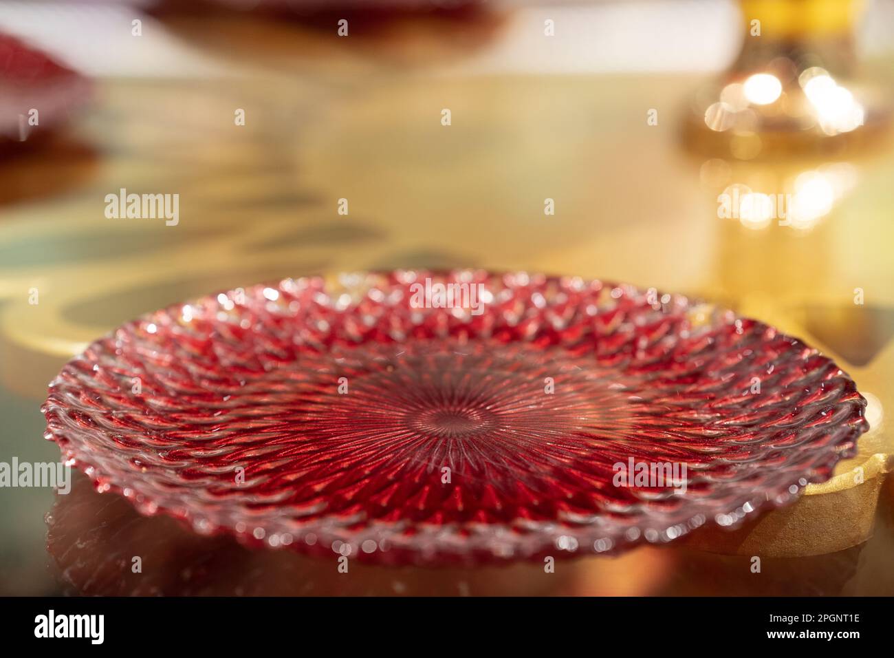 A high-gloss, red-tinted circular glass plate with a reflective surface ...