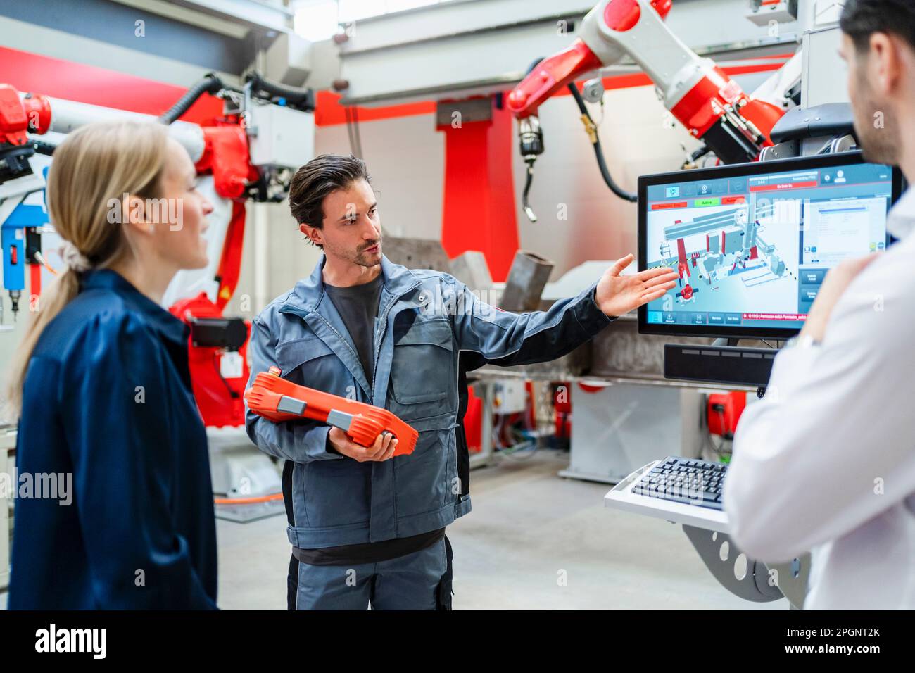 Engineer gesturing at monitor and talking to colleagues in industry ...