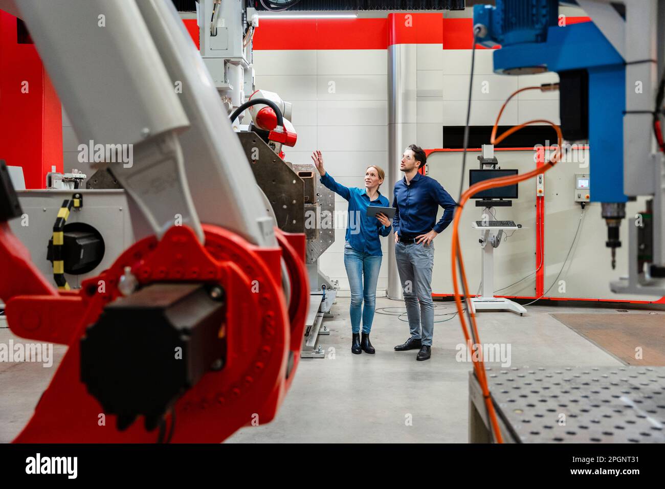 Engineer explaining colleague standing in robot factory Stock Photo - Alamy