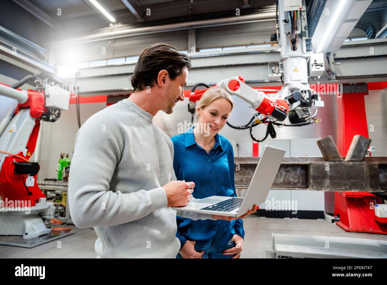 Smiling engineer standing with colleague holding laptop in robot ...