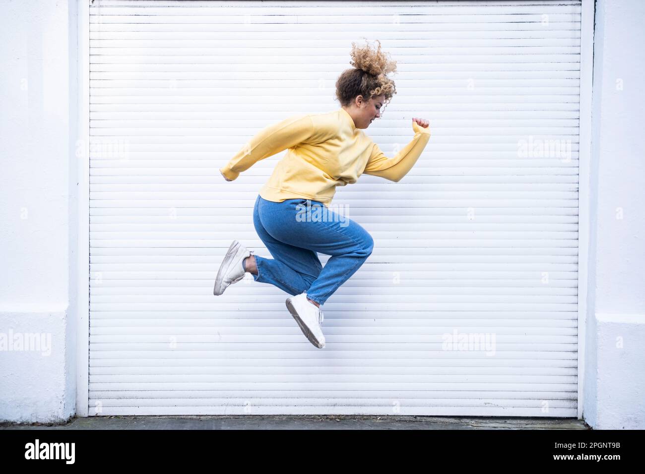 Carefree young woman jumping by white shutter Stock Photo - Alamy