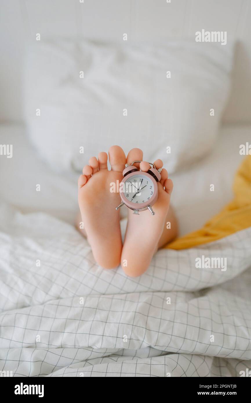 Feet of girl with alarm clock on bed at home Stock Photo - Alamy